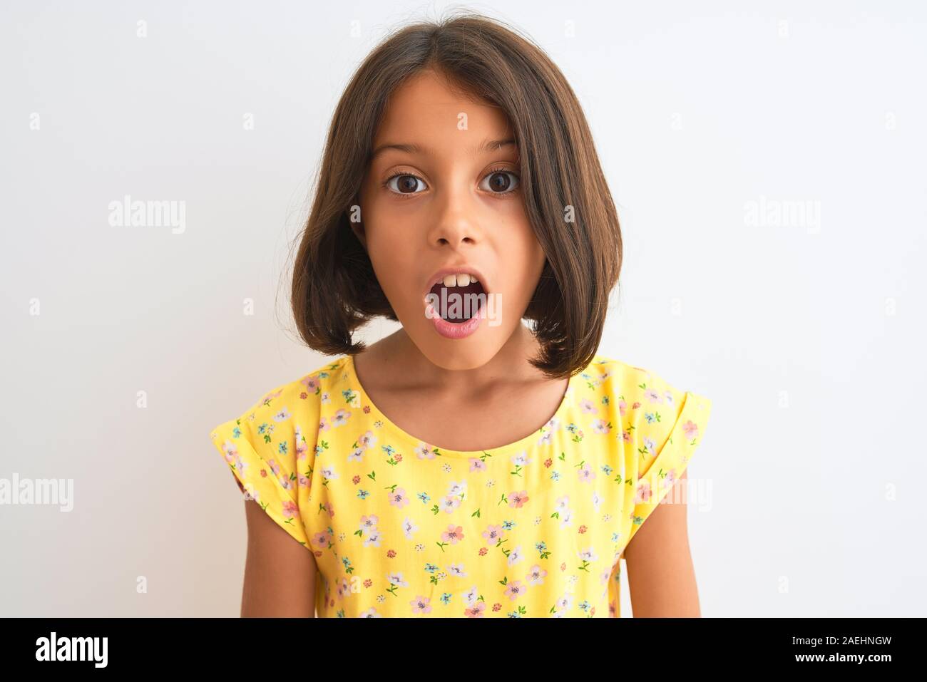 Young beautiful child girl wearing yellow floral dress standing over isolated white background ...