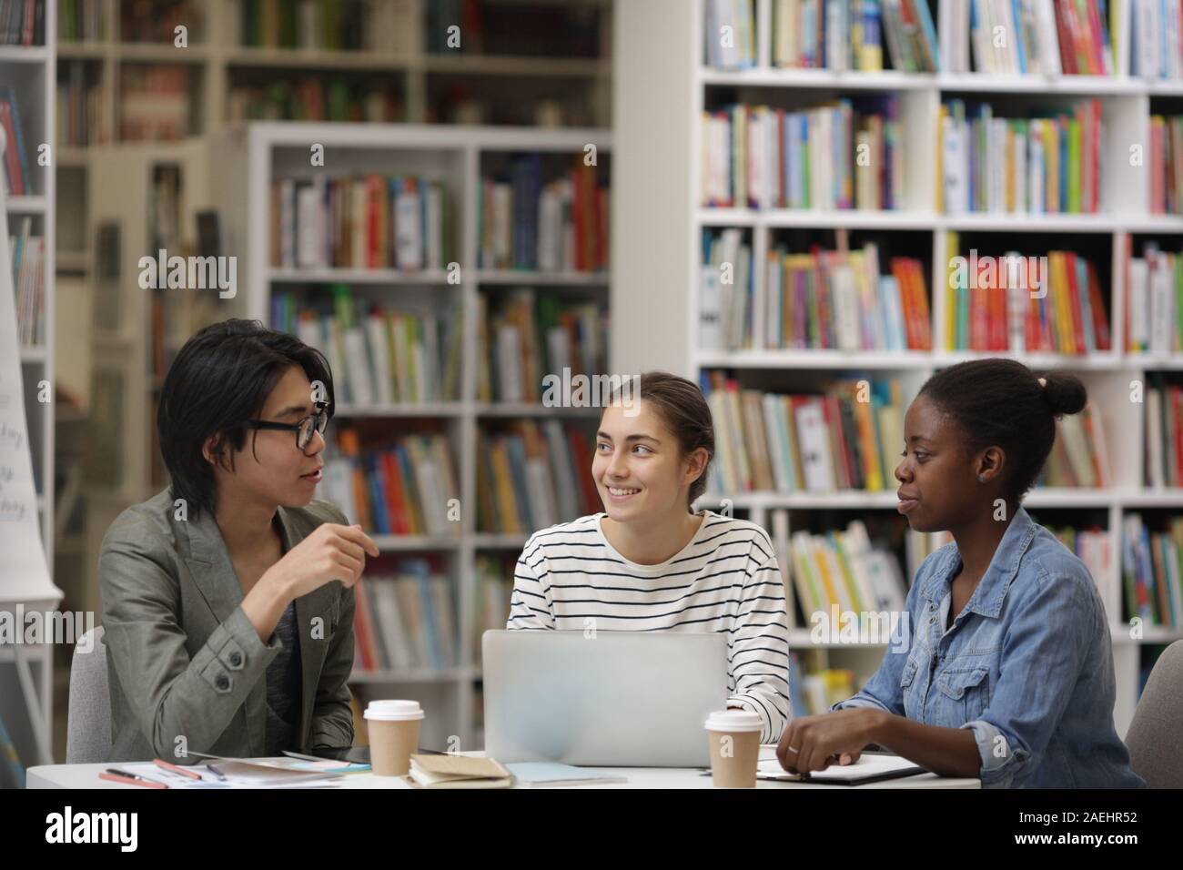 Students sitting at the table discussing teamwork using laptop and ...