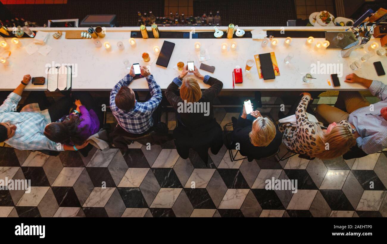 Above-view of a line of people at a bar looking at their cell phones ...