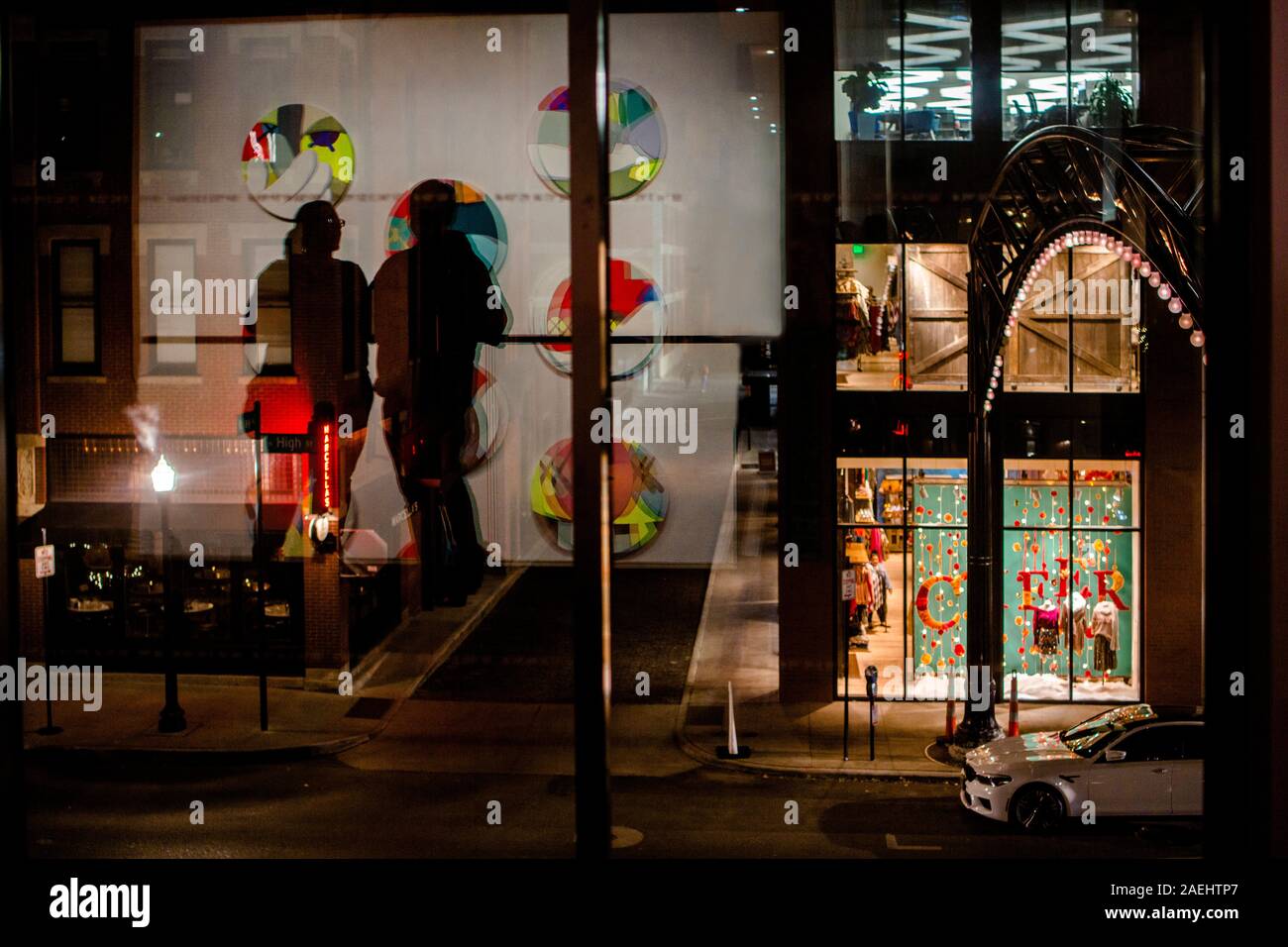 A silhouetted couple stand in a window overlooking a city at night ...