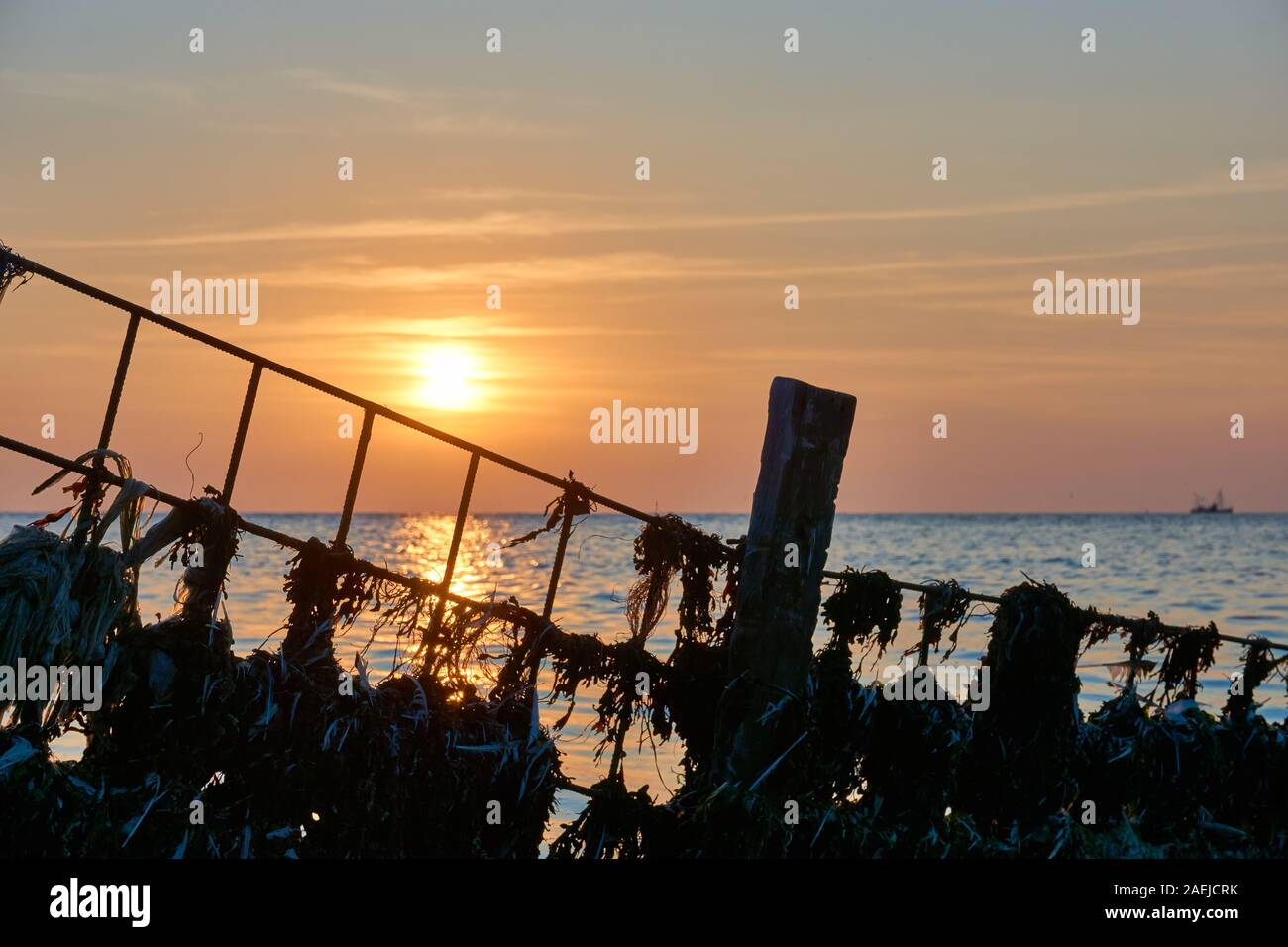 Silhouette of a metal structure with plastic waste and seaweed in front ...