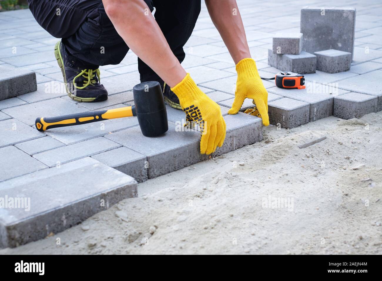 The master in yellow gloves lays paving stones in layers. Garden brick ...