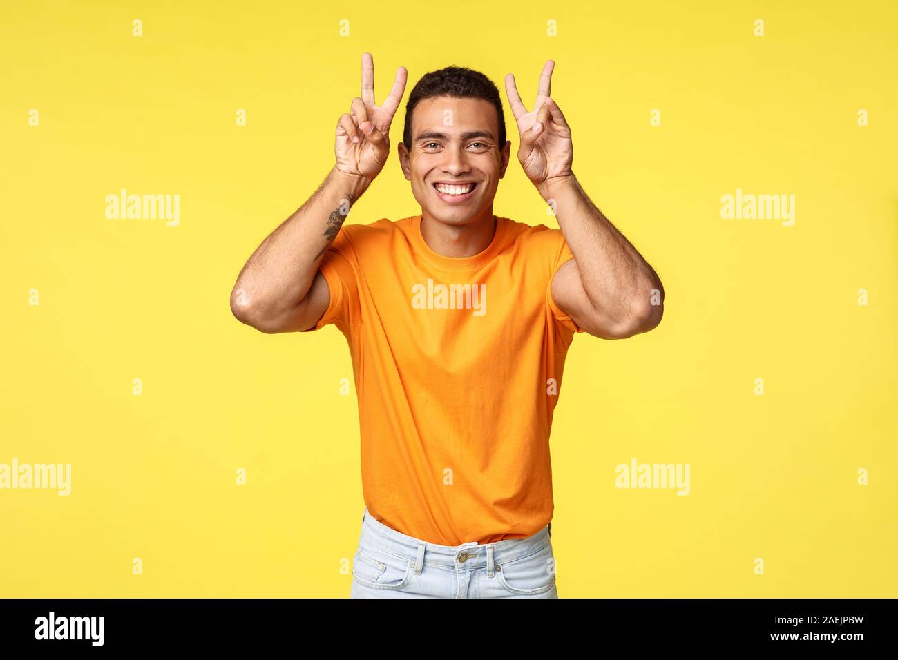 Happy, cute lovely hispanic boyfriend in orange t-shirt, showing peace ...
