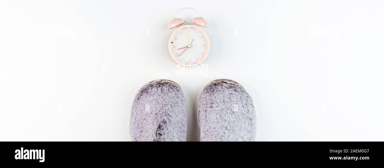 Flat lay with Soft fluffy slippers gray color and pink alarm clock ...
