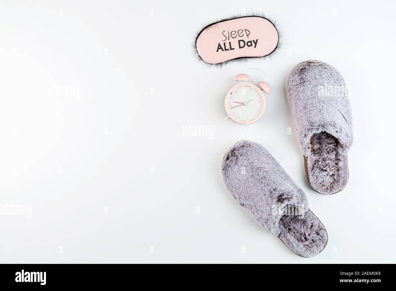 Flat lay with Soft fluffy slippers gray color, blindfold and pink alarm ...