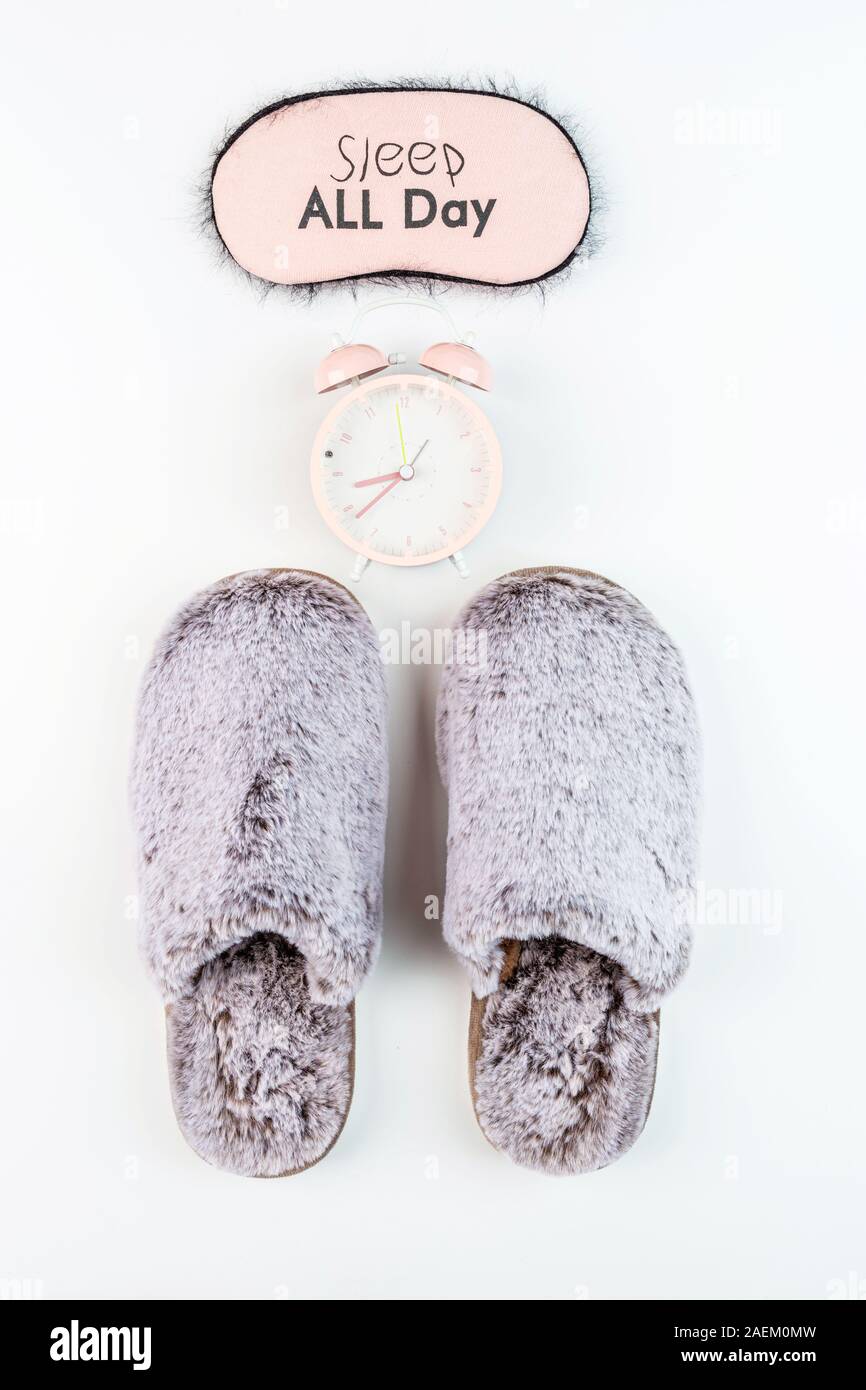 Flat lay with Soft fluffy slippers gray color and pink alarm clock ...