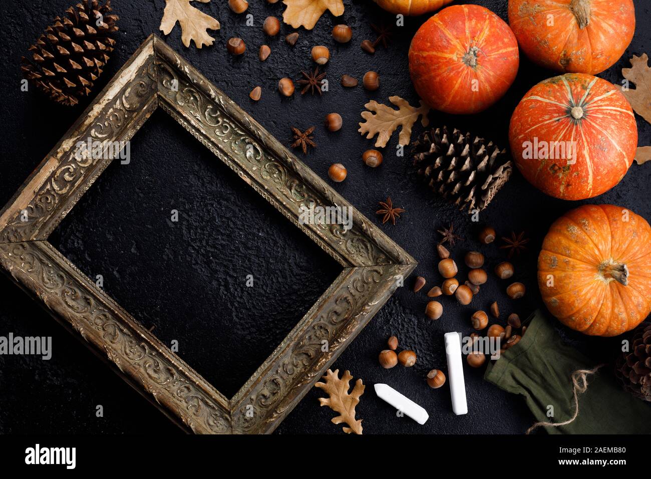 Autumn frame of pumpkins, tree leaves, hazelnuts on a black textural ...