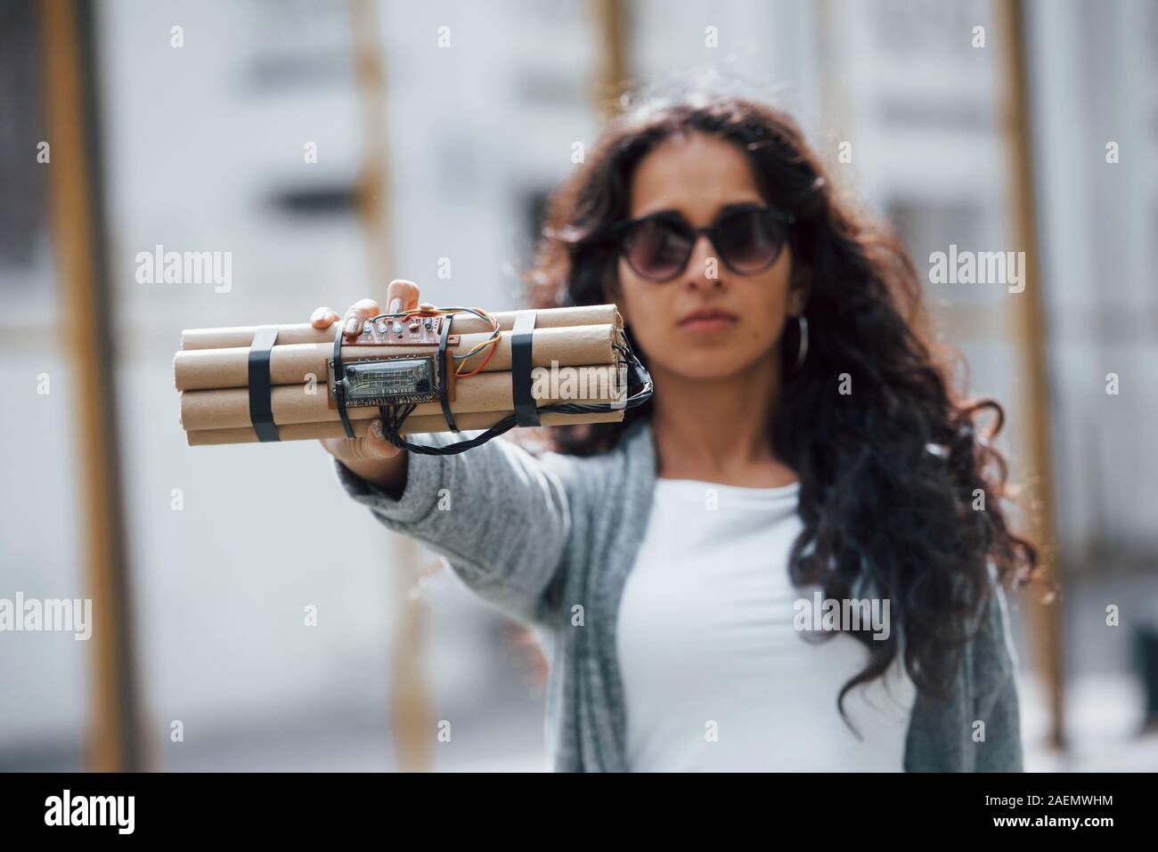 Serious girl in eyewear. Showing time bomb. Young woman holding ...
