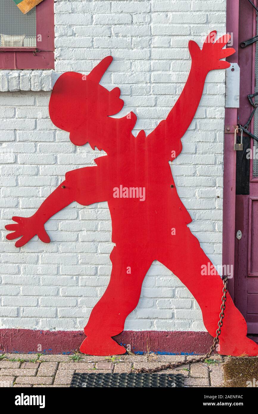 red colored comic strip figure hanging on a white brick wall of a ...