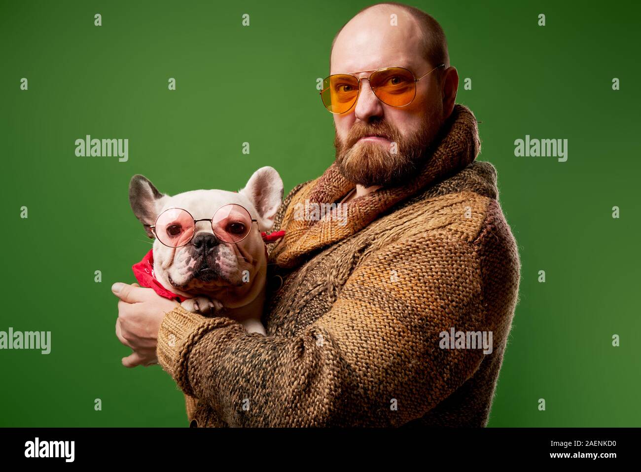 Serious man in glasses with french bulldog in his arms on empty green ...