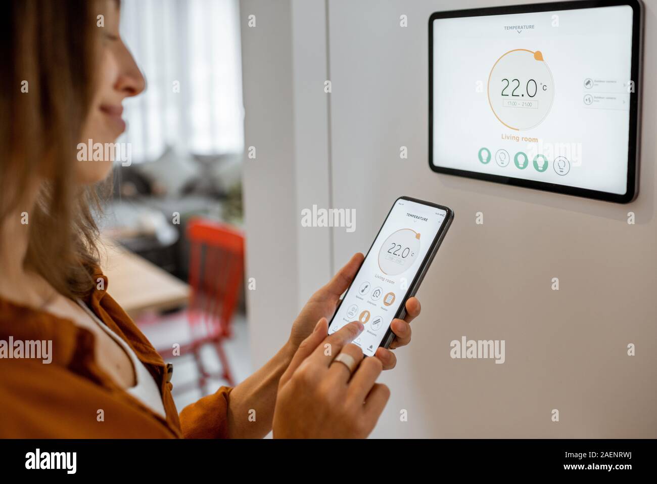 Young woman controlling temperature in the living room with smart phone ...