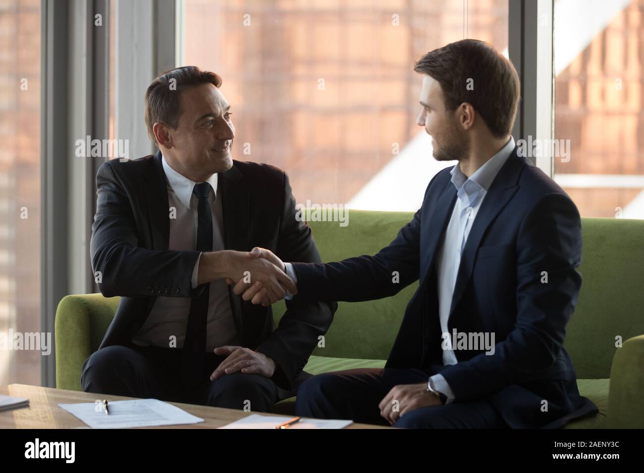 Smiling businessmen in suits handshaking, celebrating contract signing ...