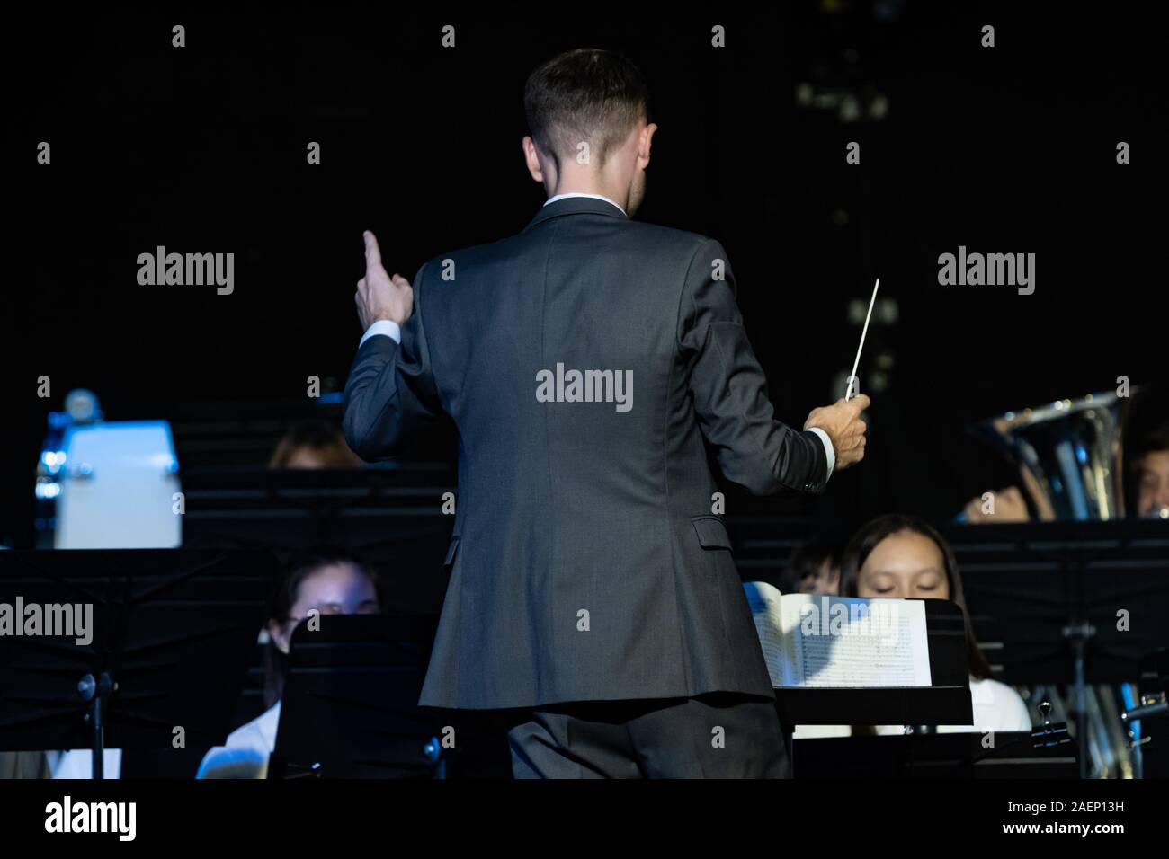 Back view of a male band conductor in formal suit conducting his ...