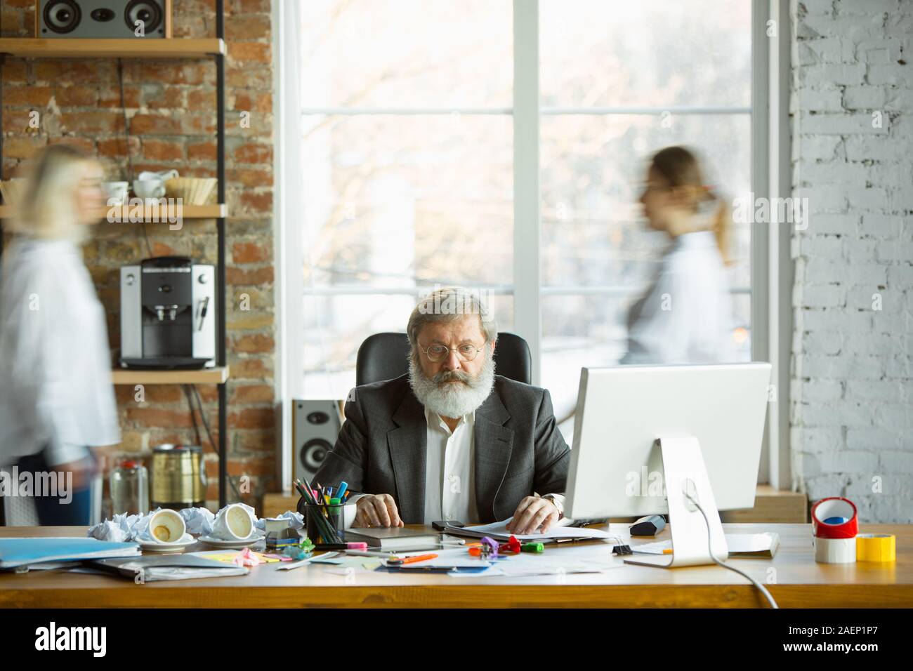 Nervous and tired boss at his workplace busy while people moving near ...