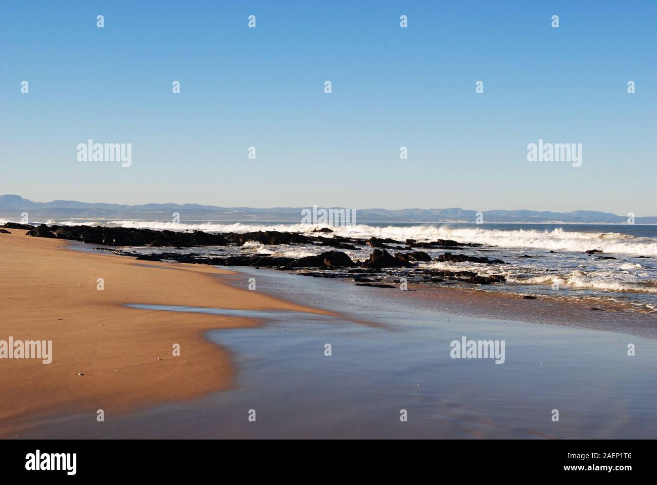 Blue sky beach with dark rocks Stock Photo - Alamy