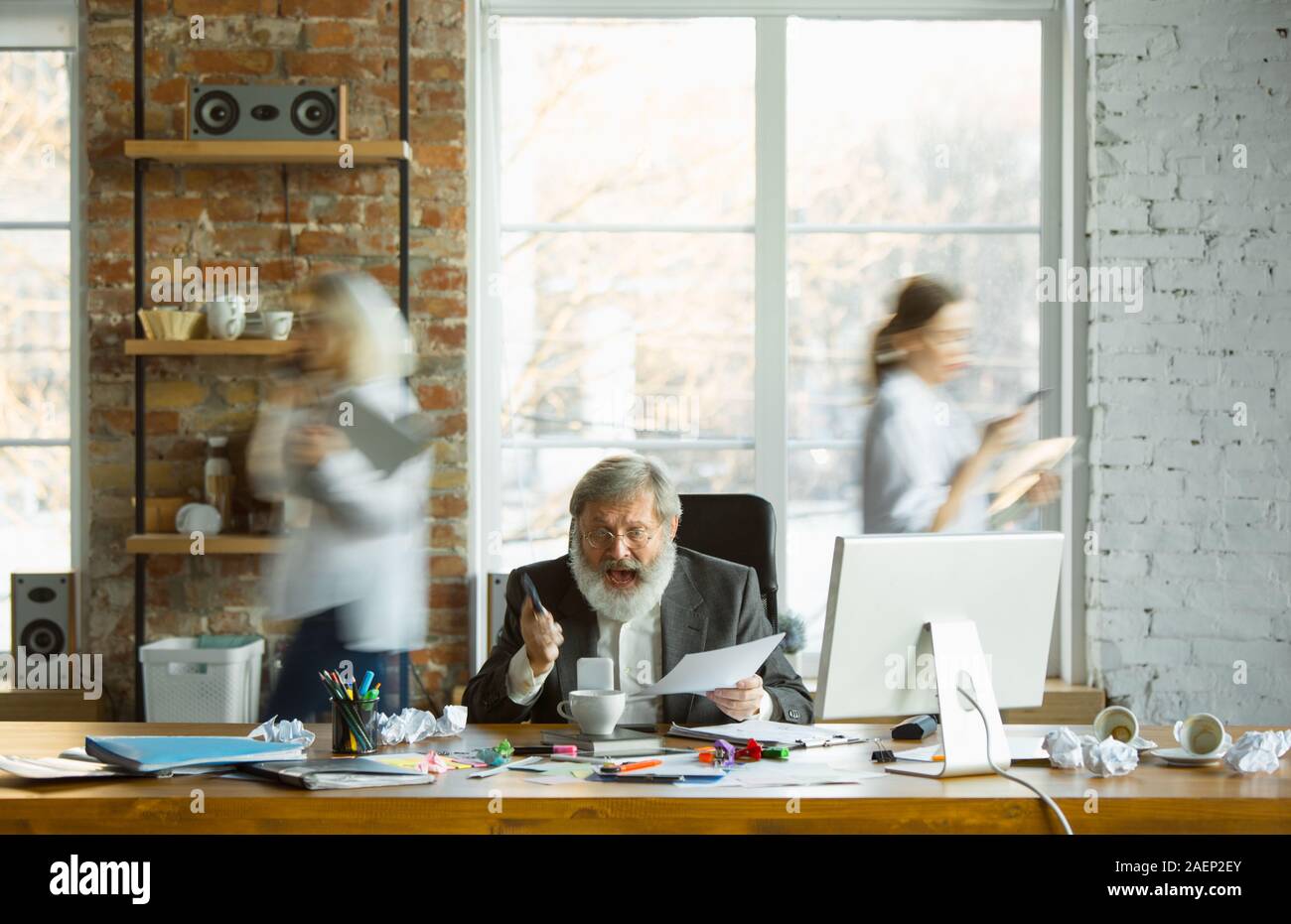 Nervous and tired boss at his workplace busy while people moving near ...