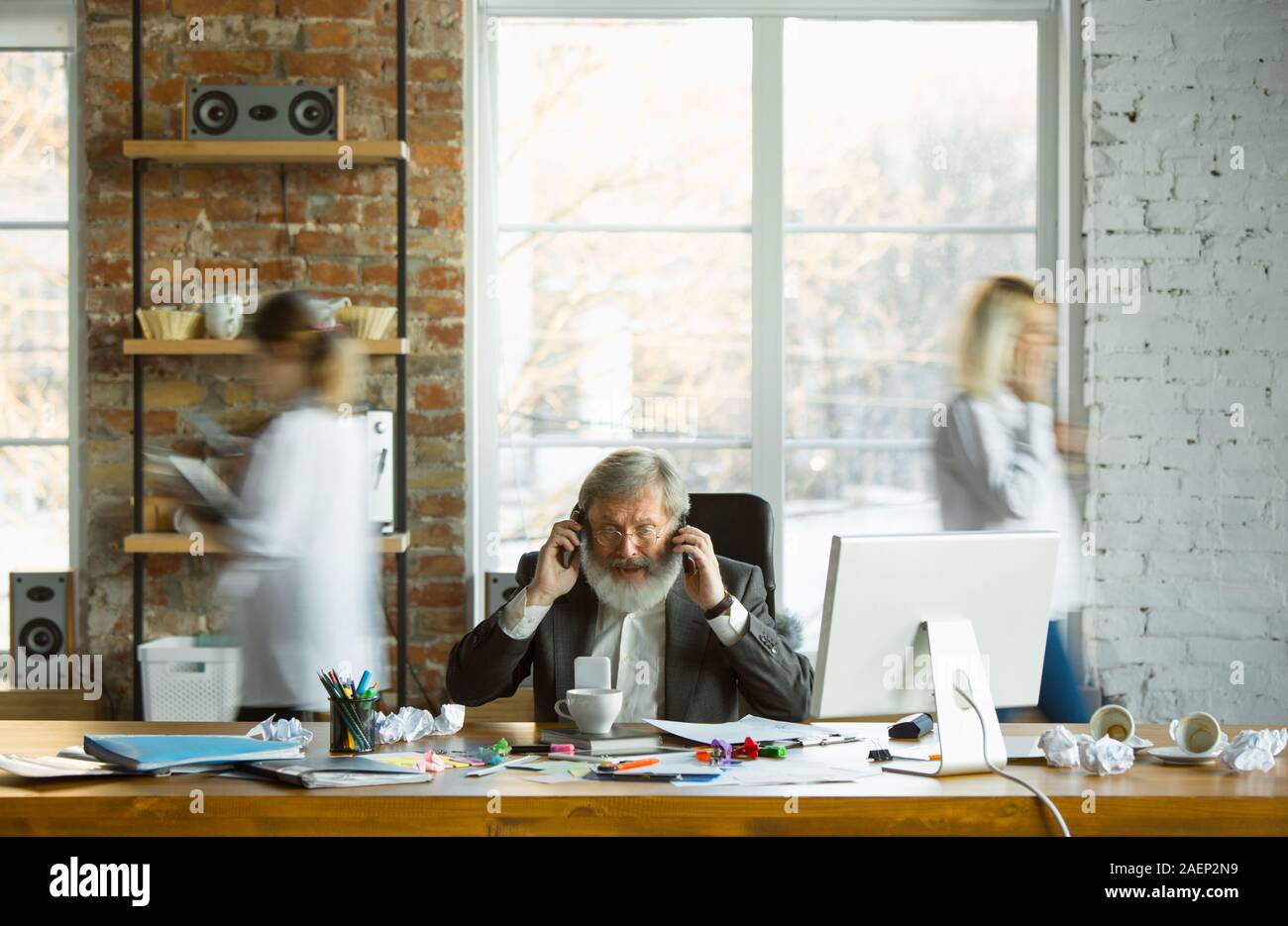 Nervous and tired boss at his workplace busy while people moving near ...