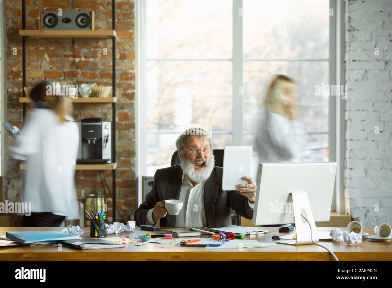 Nervous and tired boss at his workplace busy while people moving near ...