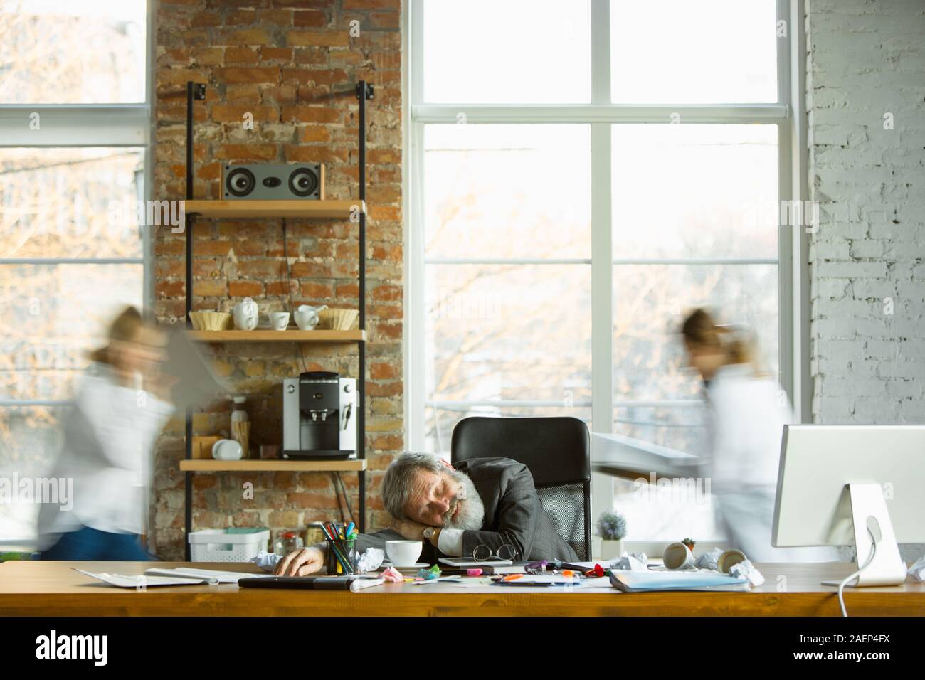 Tired boss resting at his workplace while busy people moving near ...