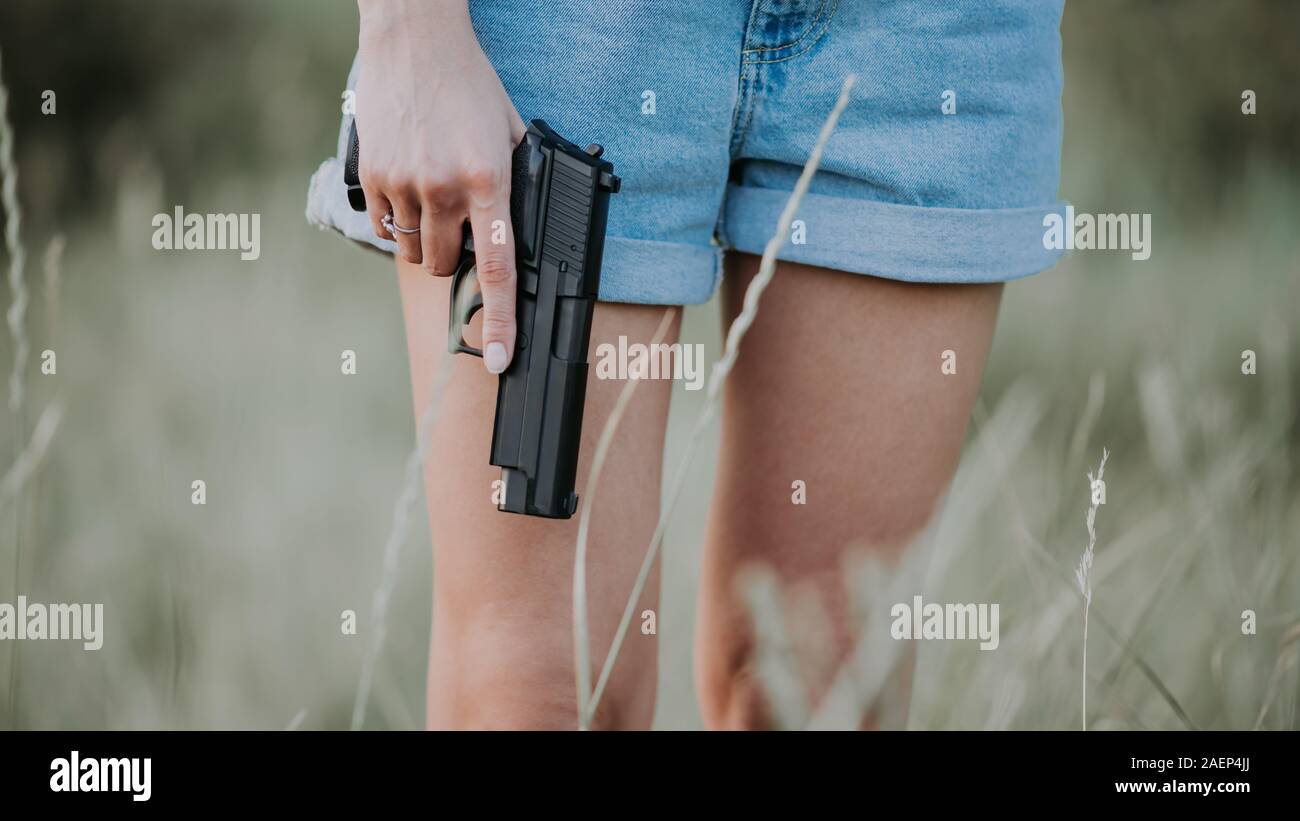 girl in denim shorts and with a gun in his hand posing in the field ...