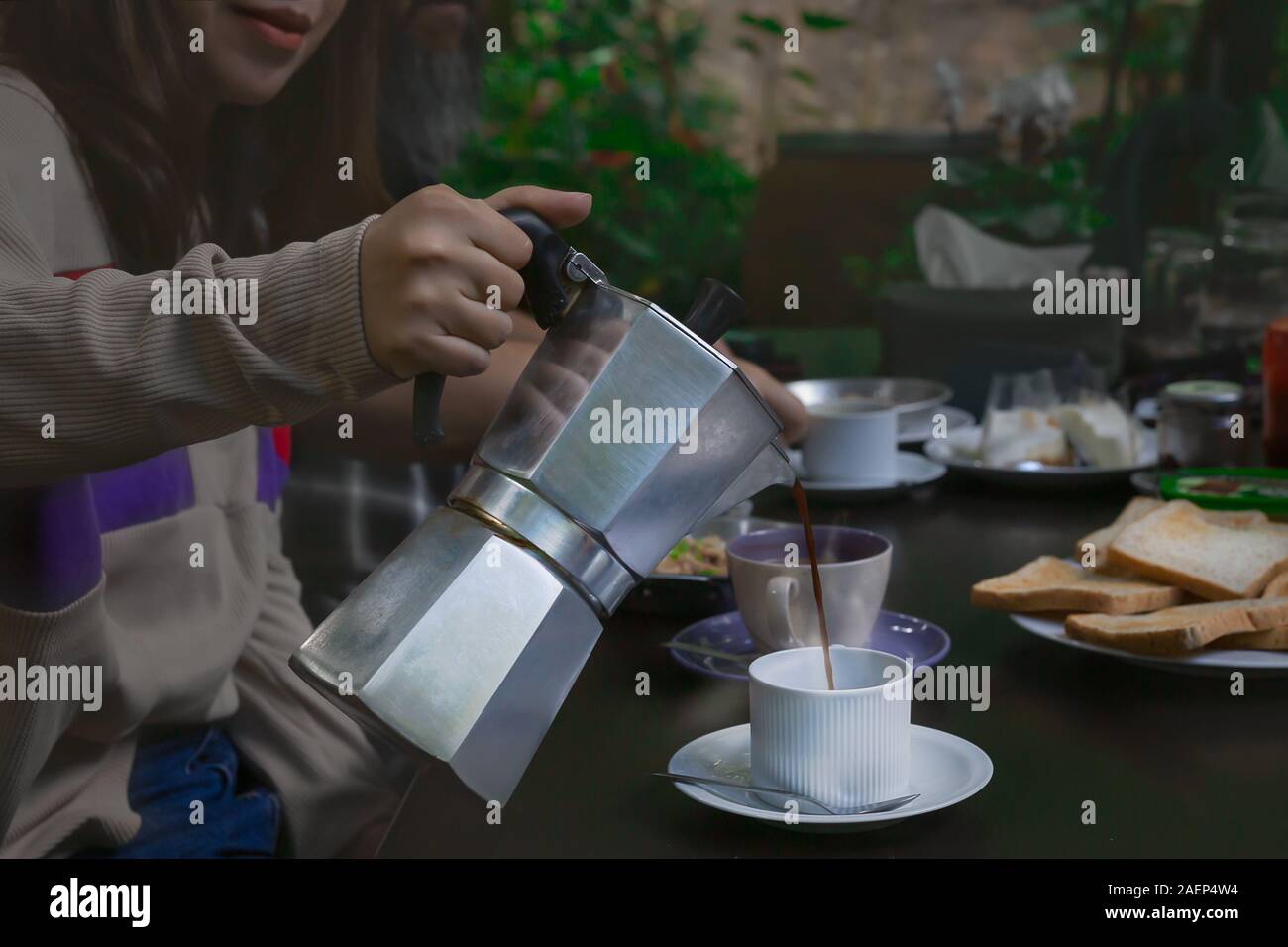 Young woman pouring coffee into a cup from coffee maker at breakfast ...