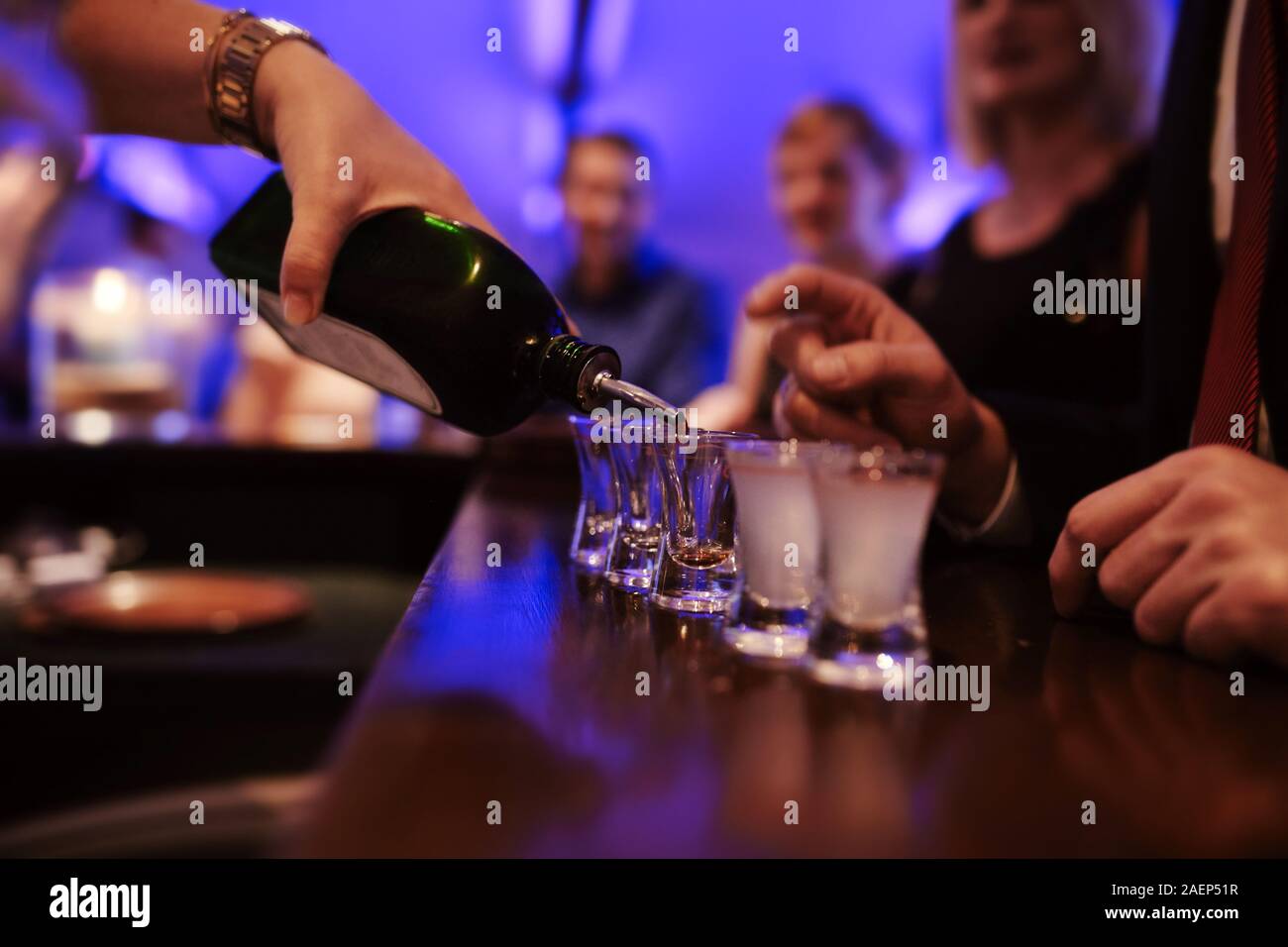 Bartender pouring strong alcoholic drink into small glasses on bar ...