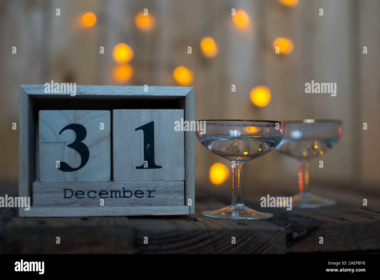 Cube wooden calendar showing date on 31th December with champagne glasses over bokeh background ...