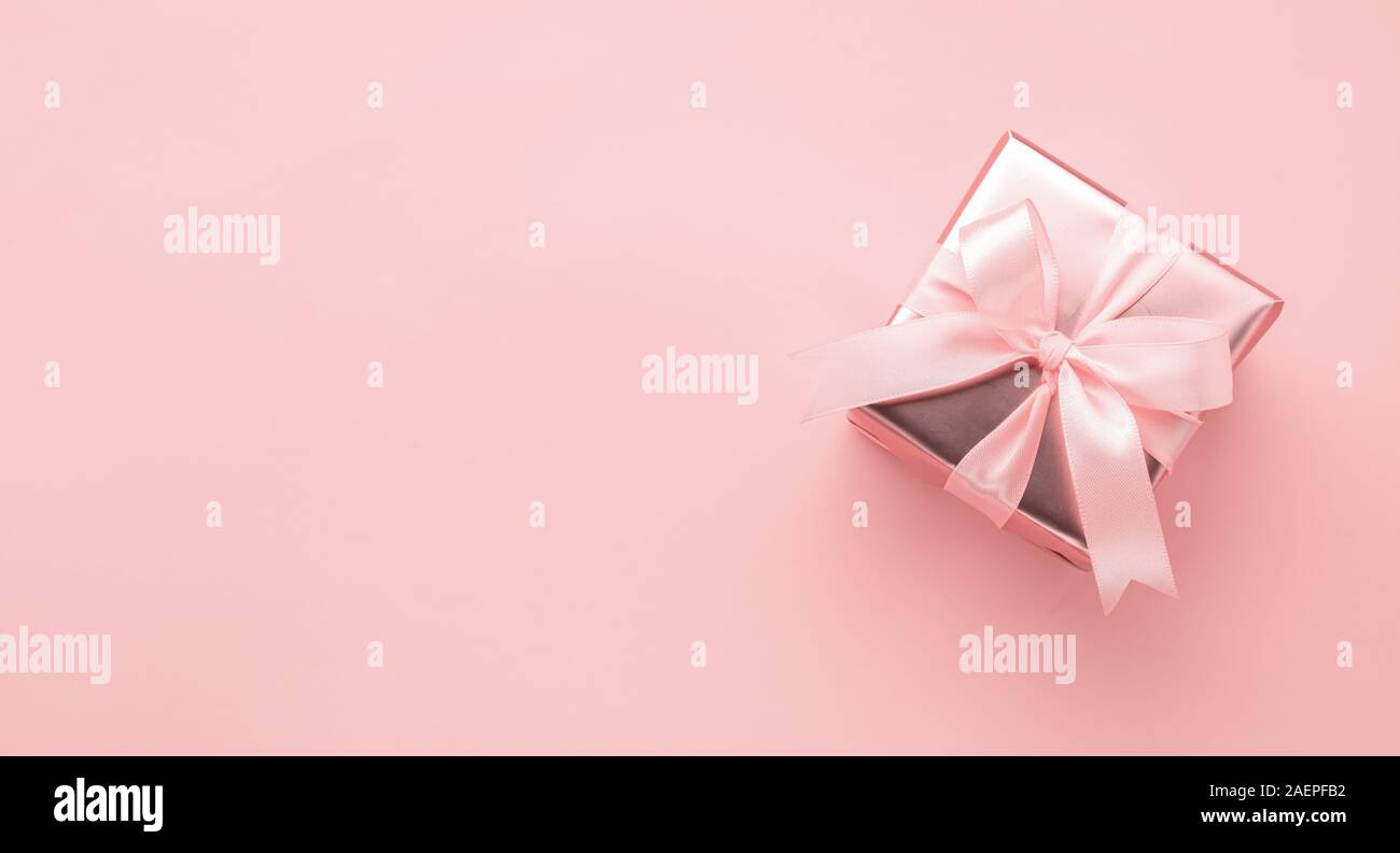 Festive box in gold packaging with a satin bow on a pastel pink ...