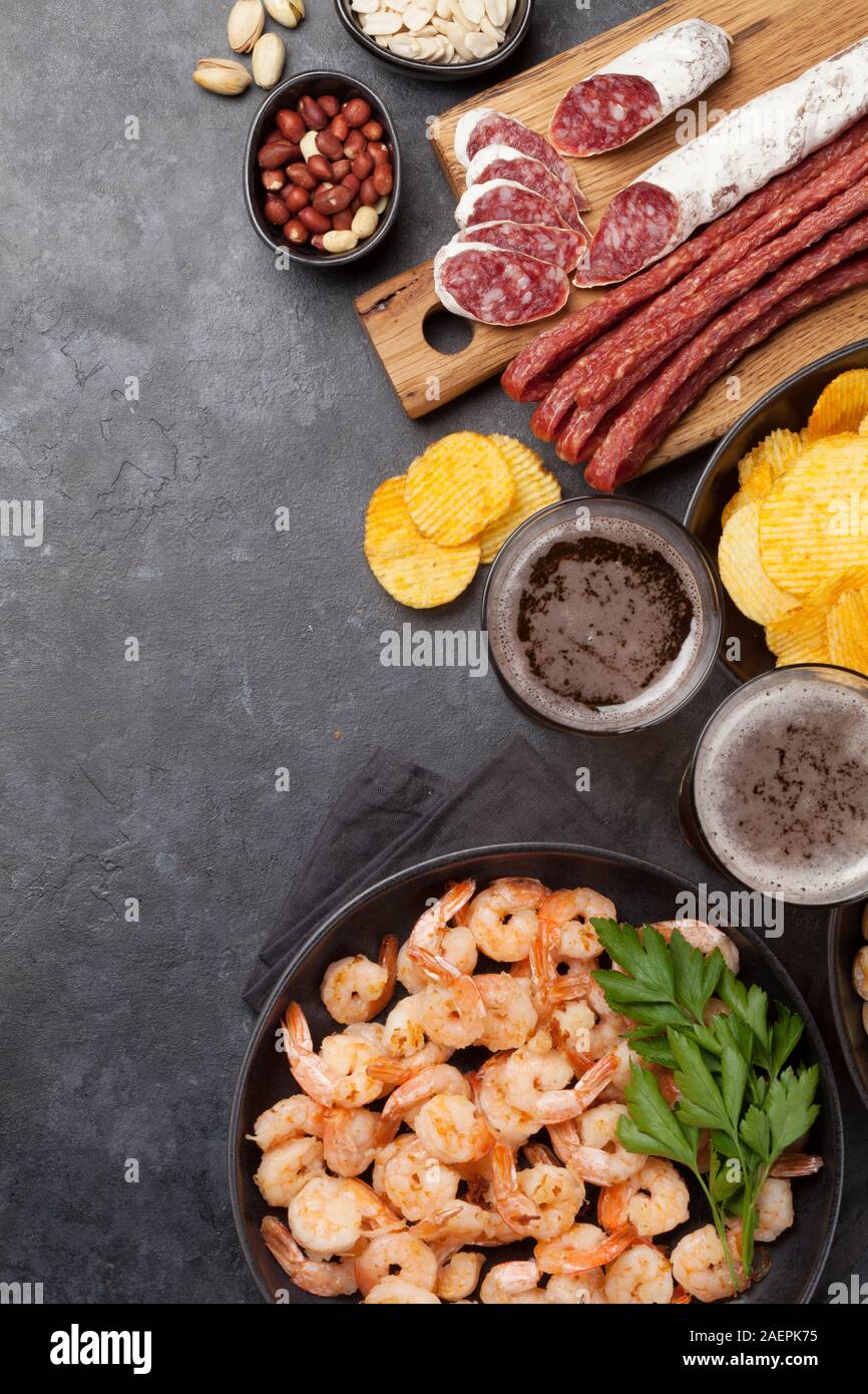 Draft beer and snacks on stone background. Nuts, chips, sausages and ...