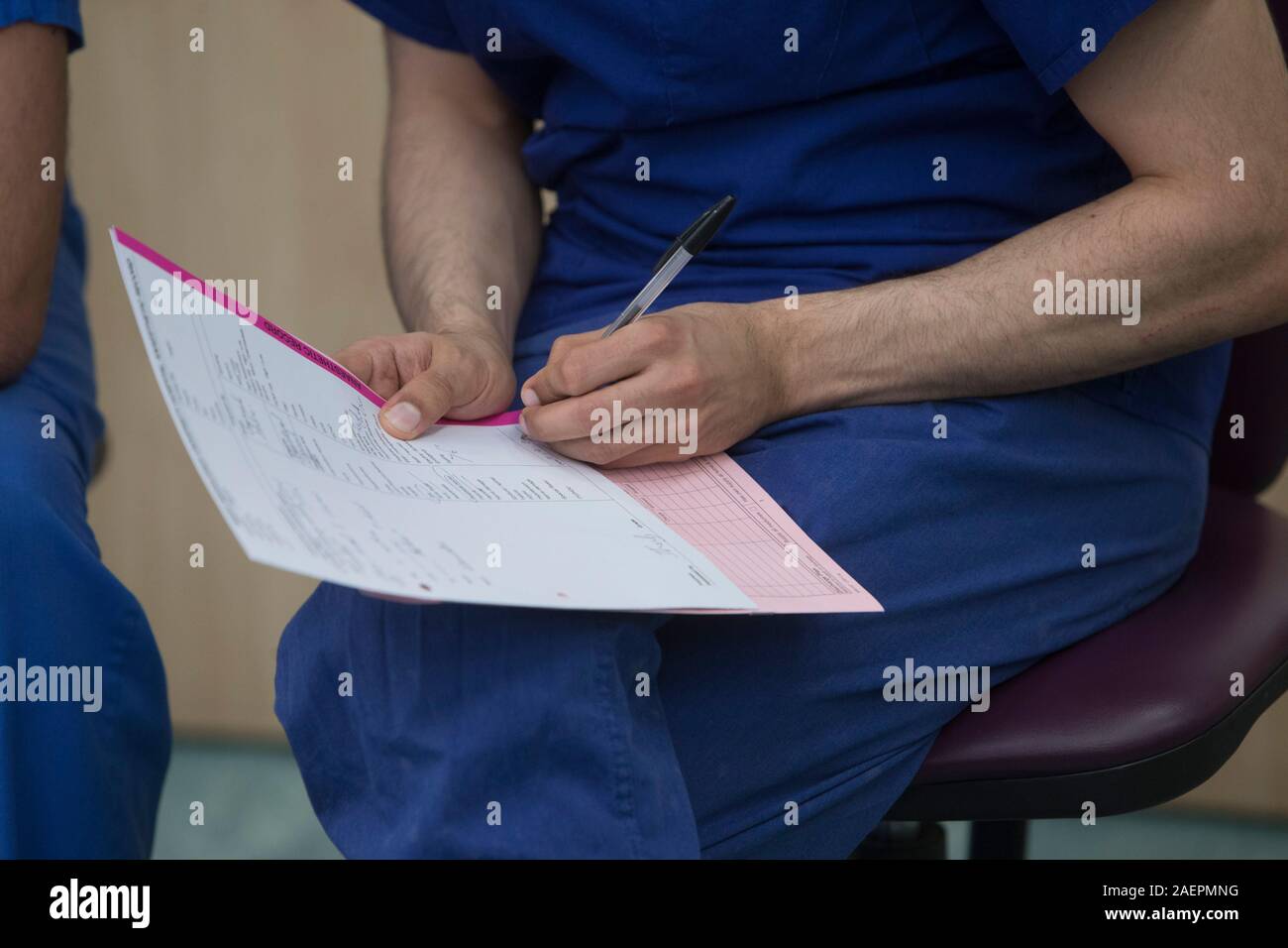 A nurse in an NHS operating theatre updates the patient notes during a ...