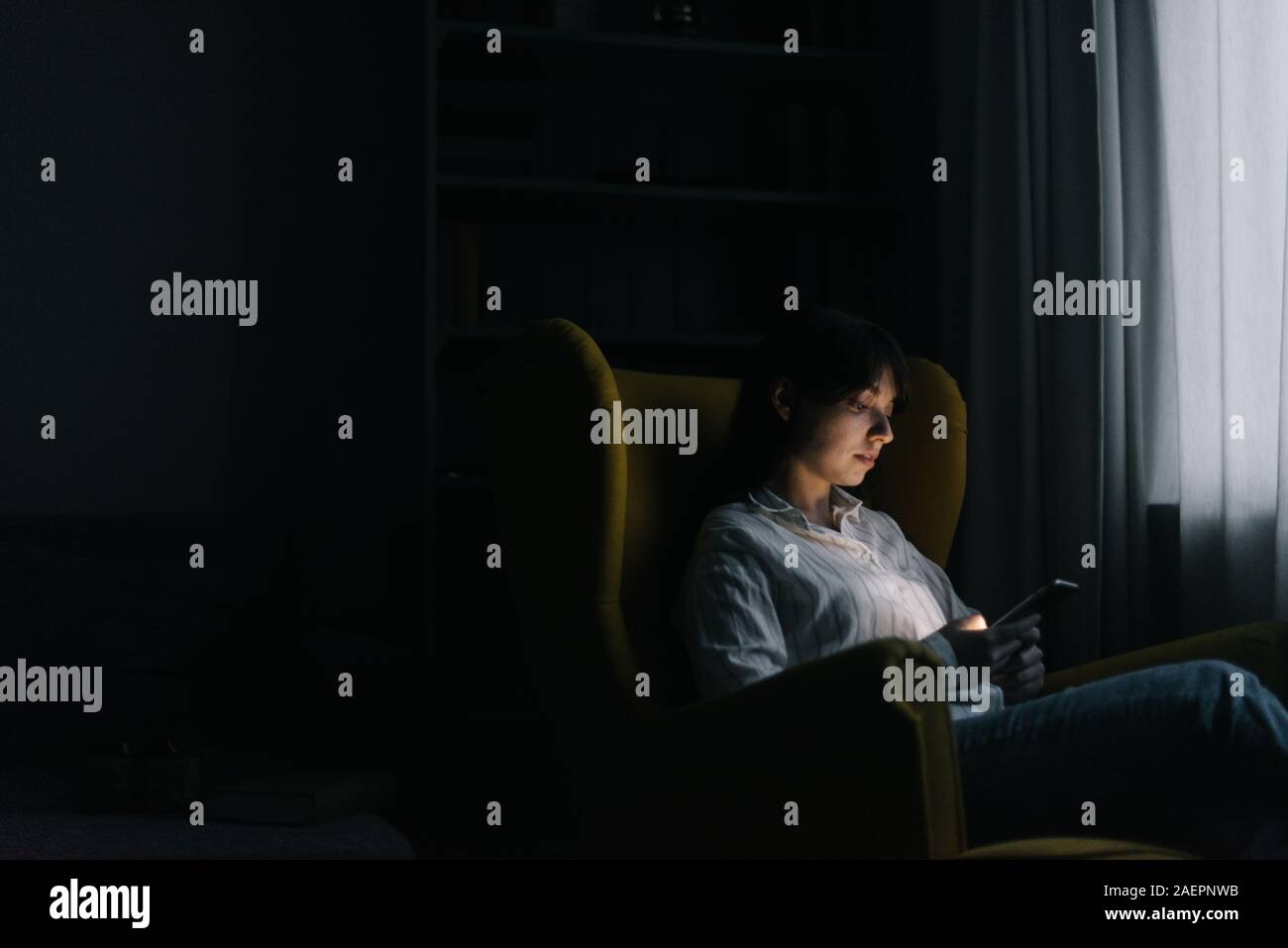 Pretty young woman is using phone in dark room Stock Photo - Alamy