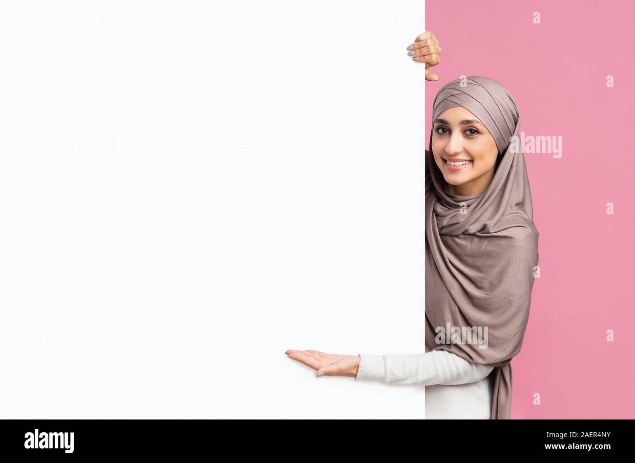 Beautiful muslim girl in hijab pointing at white blank advertisement ...