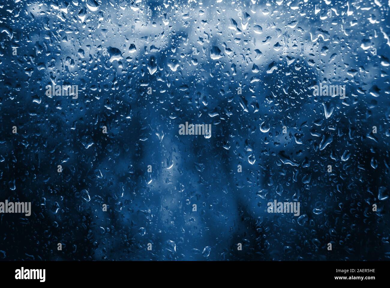Classic blue toned Spring Rain drops on window and tree in background ...