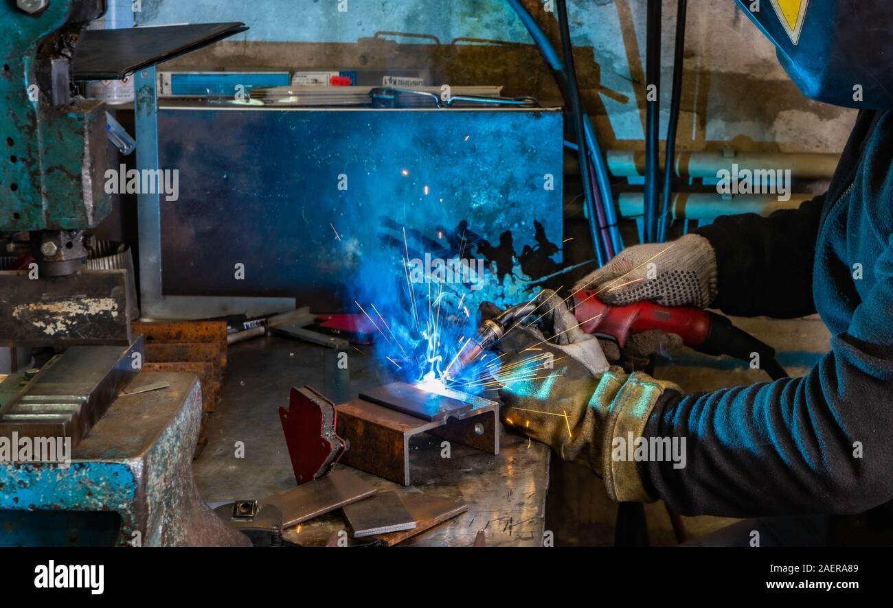 Electric welding process. Worker in welding mask. Yellow sparks fly to ...