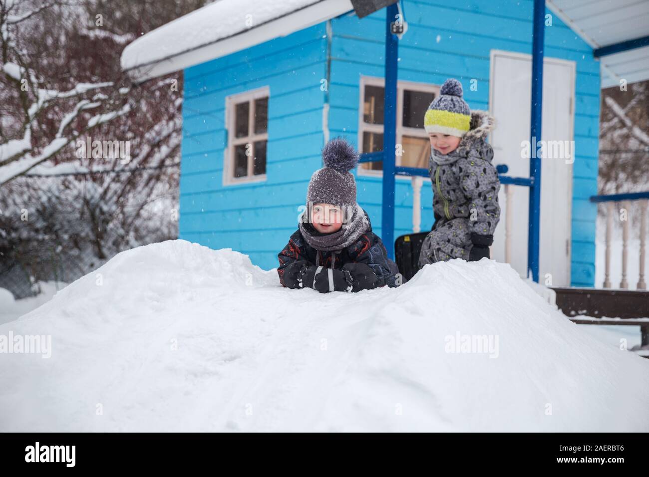 Happy children ride hill in winter in yard. Two little kids in warm ...