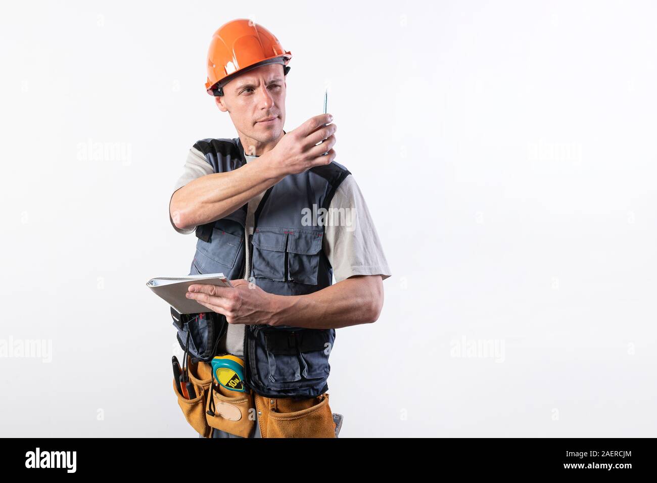 A builder in a helmet makes visual measurement with a marking pencil ...