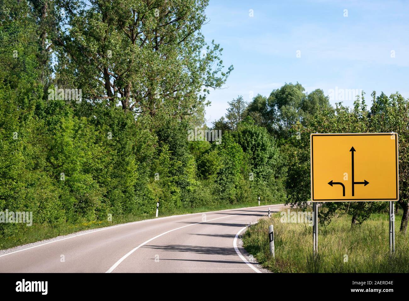 Crossroad warning sign on the side of an empty street in spring scenery ...