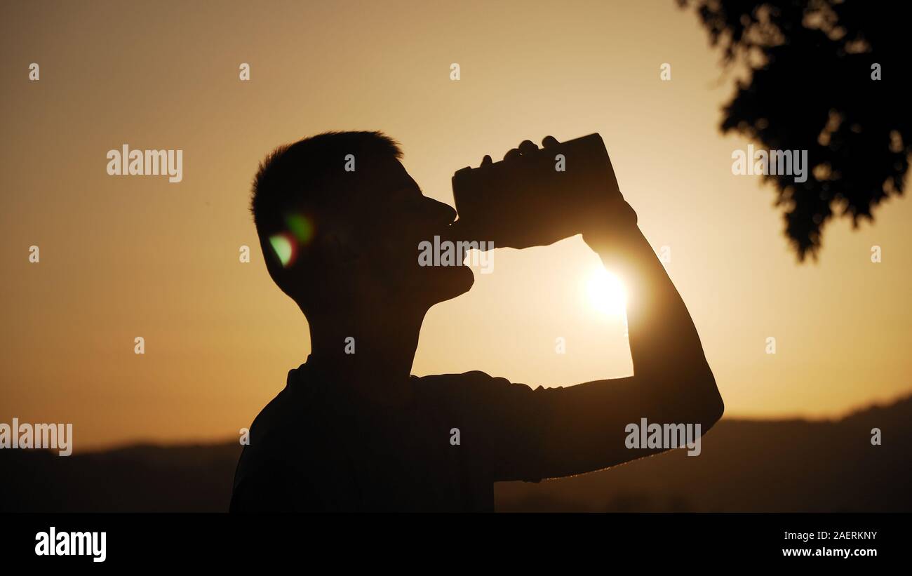 silhouette of fit young man drinking water with sun behind it in sunset ...