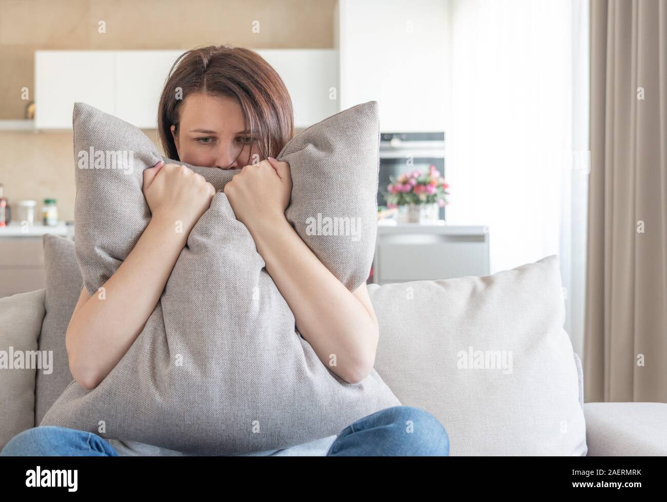 Sad depressed woman at home, she is sitting on the couch and hugging a ...