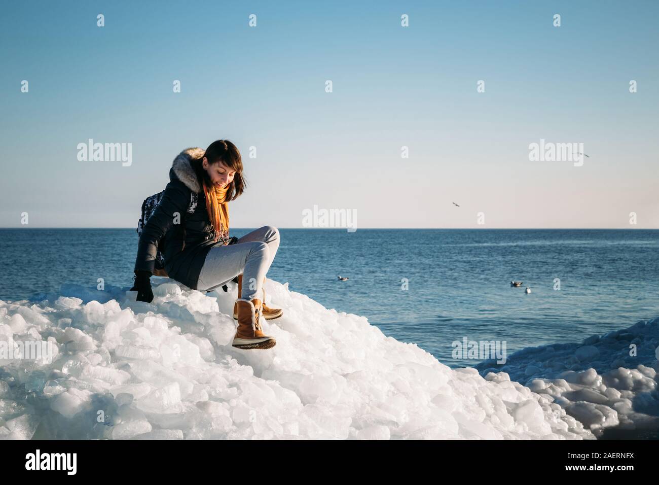 Young smiling woman sitting on a top of frozen sea ice blocks on a ...