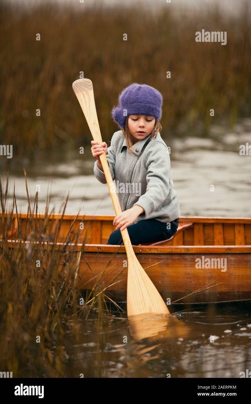 Young girl looks down as she tries to paddle a wooden canoe through ...