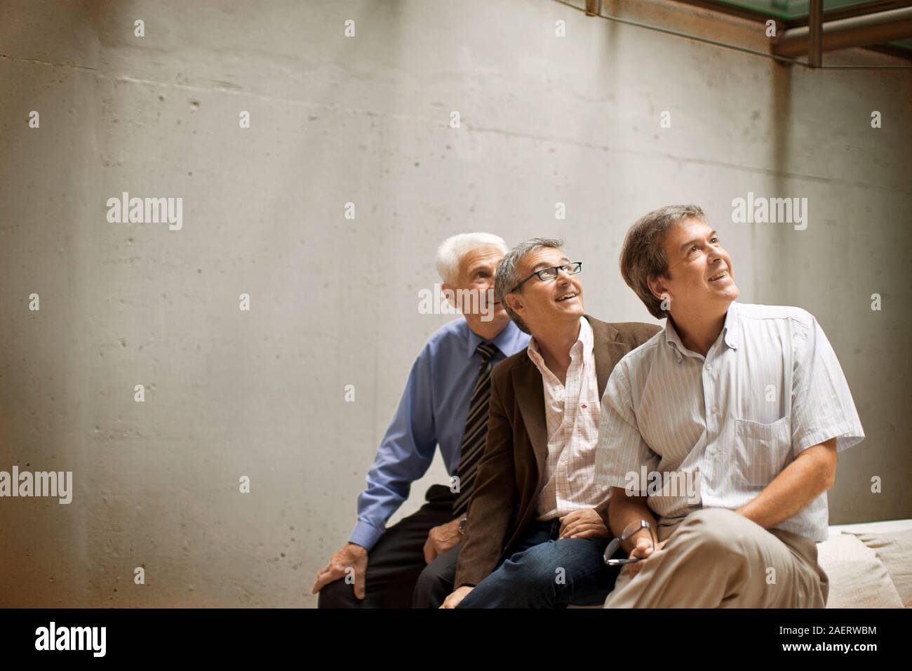 Three smiling businessmen sitting side by side look up over their ...