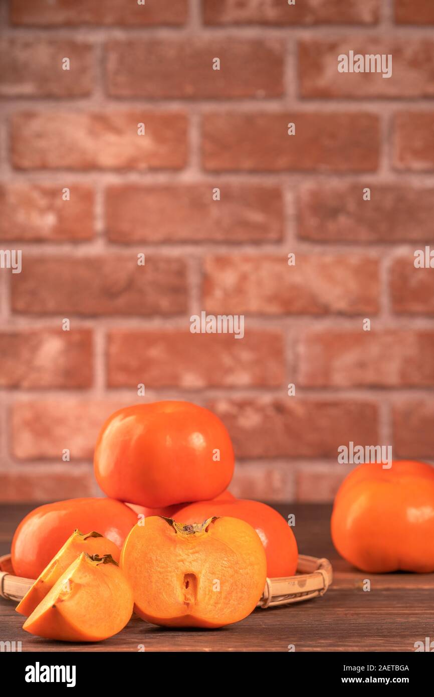 Sliced sweet persimmon kaki in a bamboo sieve basket on dark wooden ...