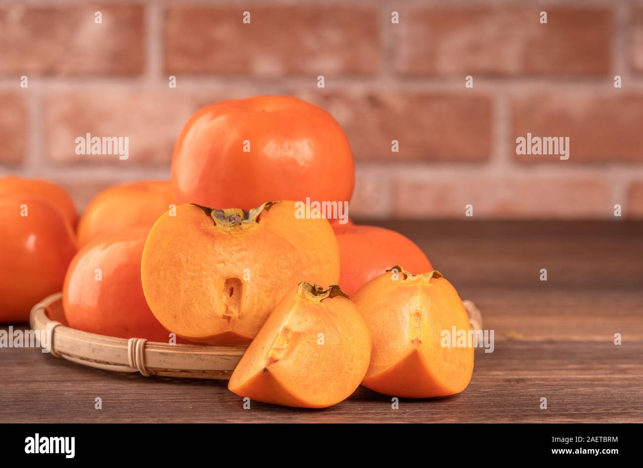 Sliced sweet persimmon kaki in a bamboo sieve basket on dark wooden ...