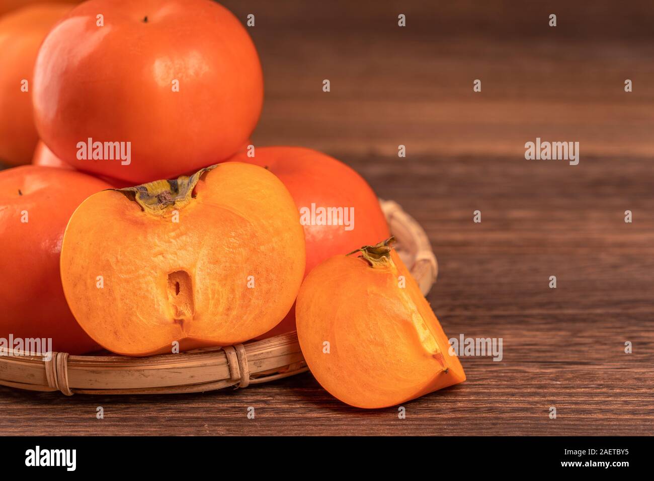 Sliced sweet persimmon kaki in a bamboo sieve basket on dark wooden ...
