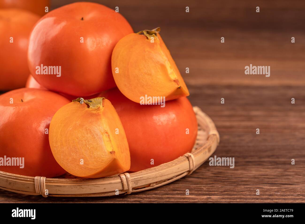 Sliced sweet persimmon kaki in a bamboo sieve basket on dark wooden ...