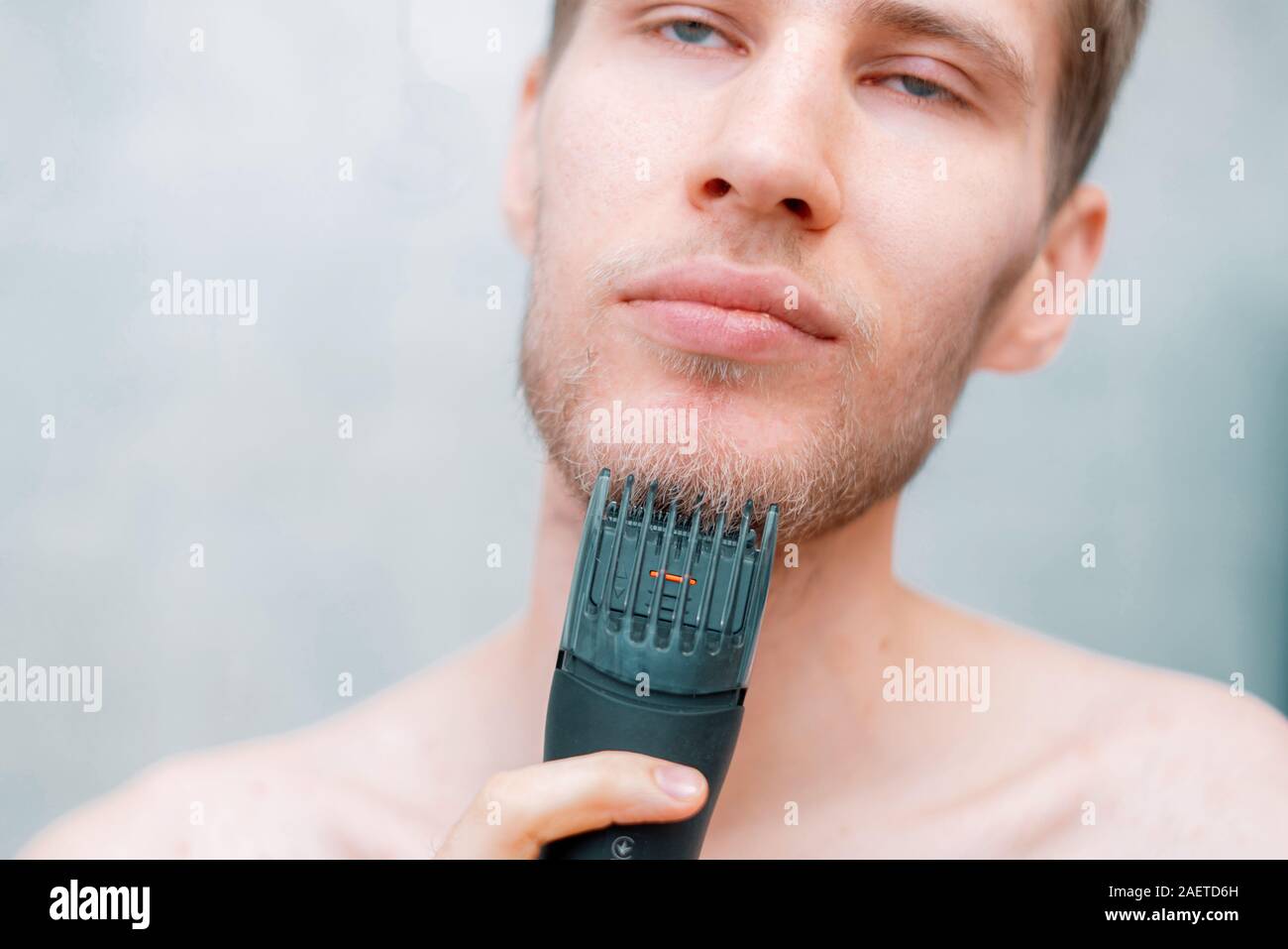 the close up of young male person cutting his beard using the trimmer ...