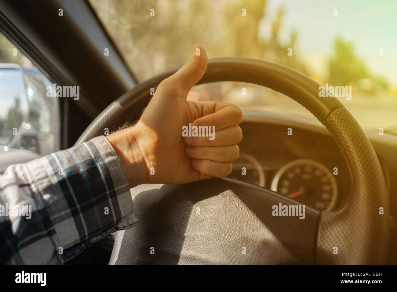 a first person view of driver showing thumb up in front of steering ...