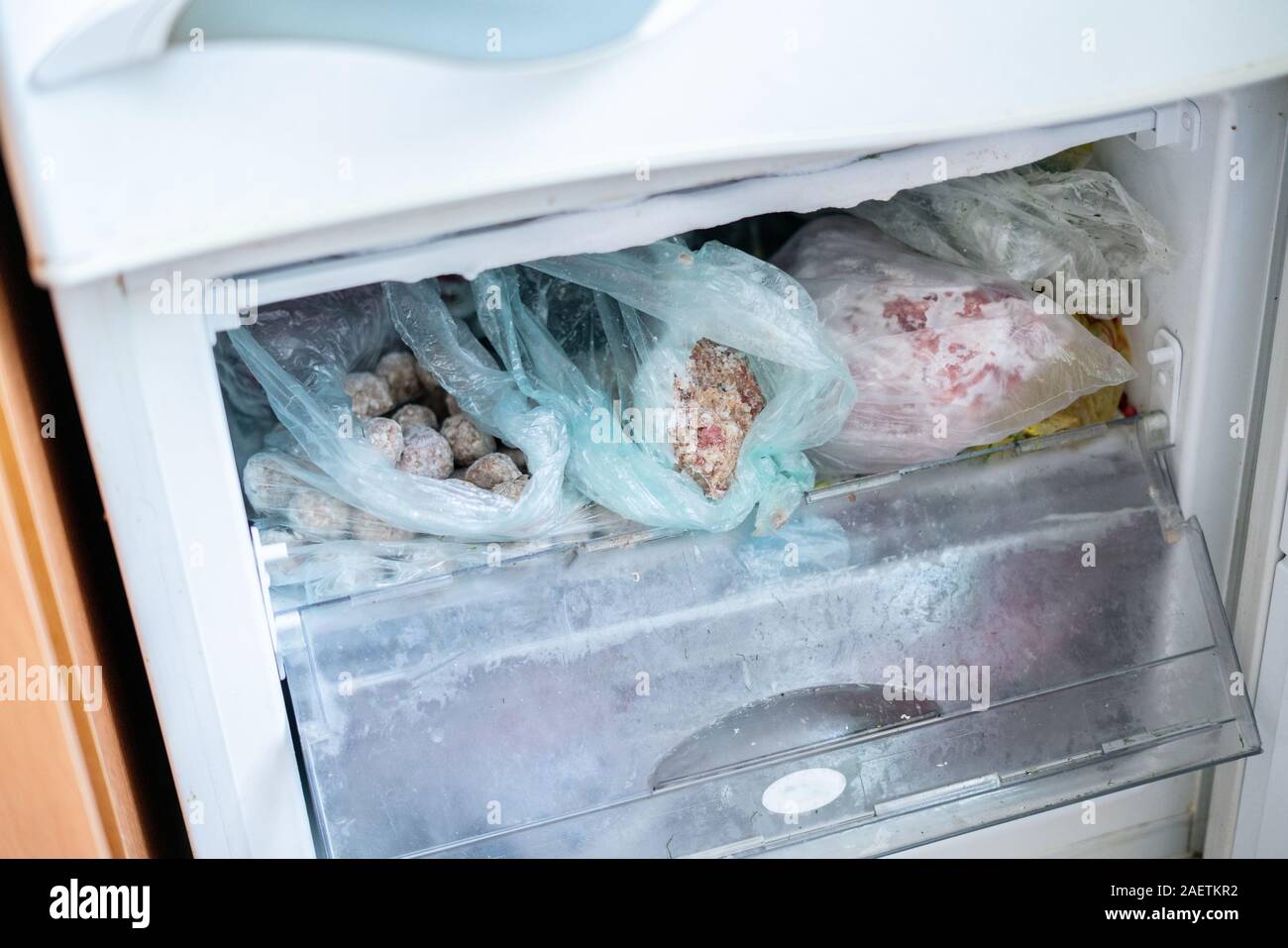 opened freezer part of the fridge with many frozen packages of food ...