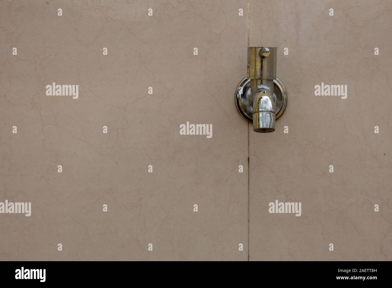 Stainless steel water tap fixed to tiled wall in building exterior ...